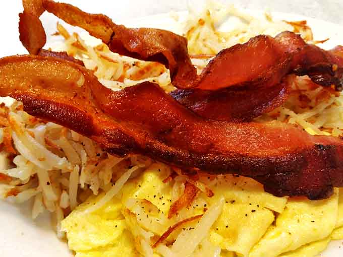 The breakfast trinity &ndash; perfectly scrambled eggs, crispy hash browns, and bacon cooked to that ideal point between chewy and crisp.