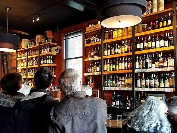 The impressive wall of spirits gleams like a liquid library, bottles standing at attention while patrons contemplate their next sip &ndash; a whiskey lover's dream realized.
