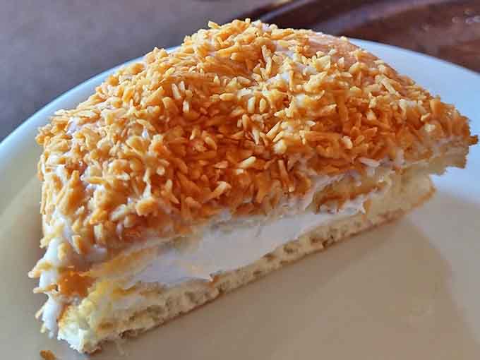 Coconut Slice: Layer upon layer of fluffy cake and cream, topped with a snowfall of toasted coconut shreds.