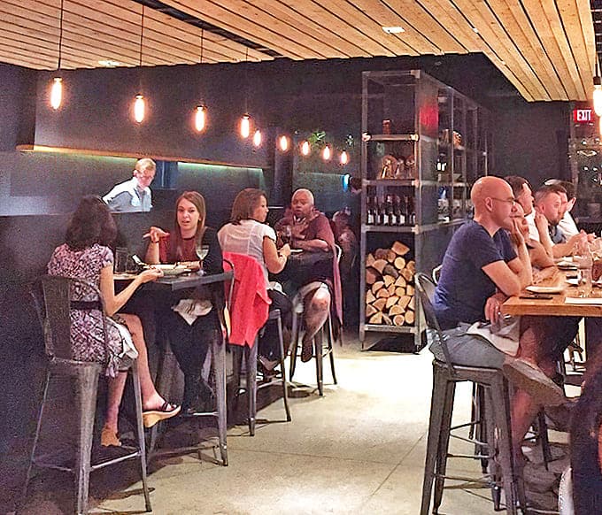 Diners: Conversation and connection happen naturally in this thoughtfully designed space. Wood-lined ceilings add warmth while pendant lights create intimate dining zones.