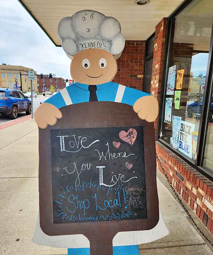 A cheerful baker mascot welcomes visitors with a chalkboard message about shopping local, because Kennedy's knows community matters as much as quality ingredients.