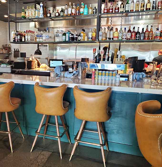 The turquoise and white bar area with caramel leather stools creates a sophisticated spot for solo diners or pre-dinner cocktails.