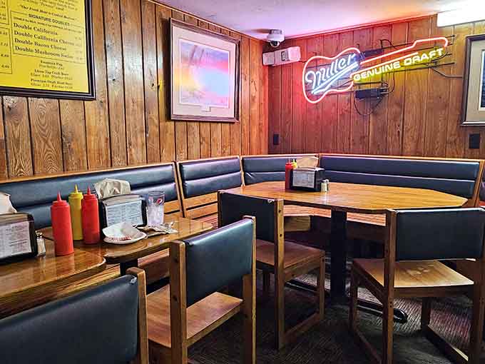 Classic booth seating with a Miller sign glowing overhead, creating the perfect spot to settle in for a meal that'll have you planning your next visit.
