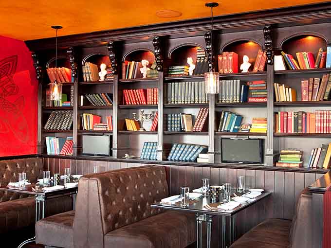 Cozy booths backed by bookshelves create intimate dining nooks where conversations flow as smoothly as the whiskey behind the bar.