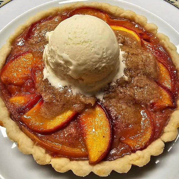 This isn't just dessert, it's a work of art. A golden crust cradling juicy peaches, topped with a scoop of ice cream that's melting faster than your willpower.