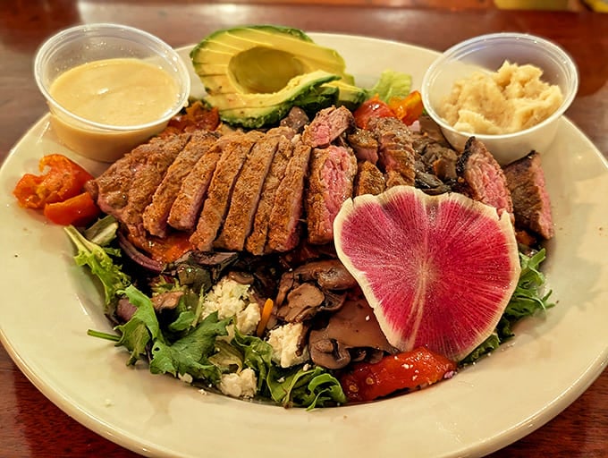 Sliced steak over fresh greens with avocado and vegetables, proving salads here are substantial meals, not diet afterthoughts or rabbit food.