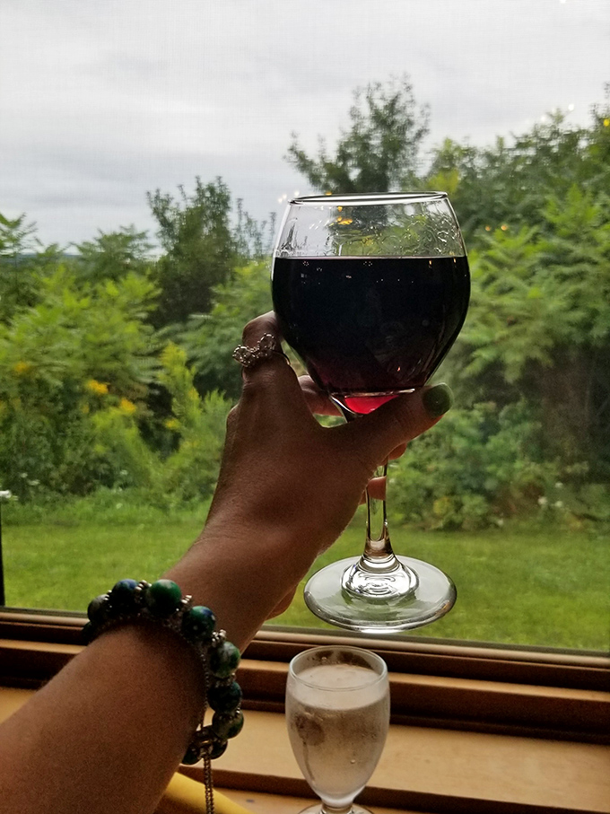 A glass of red wine held against the backdrop of Vermont's rolling hills, the perfect companion to a memorable meal.