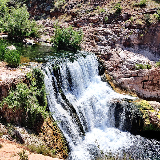 Nature's perfect composition: A small waterfall creates white foam against red rocks while emerald pools invite weary hikers.