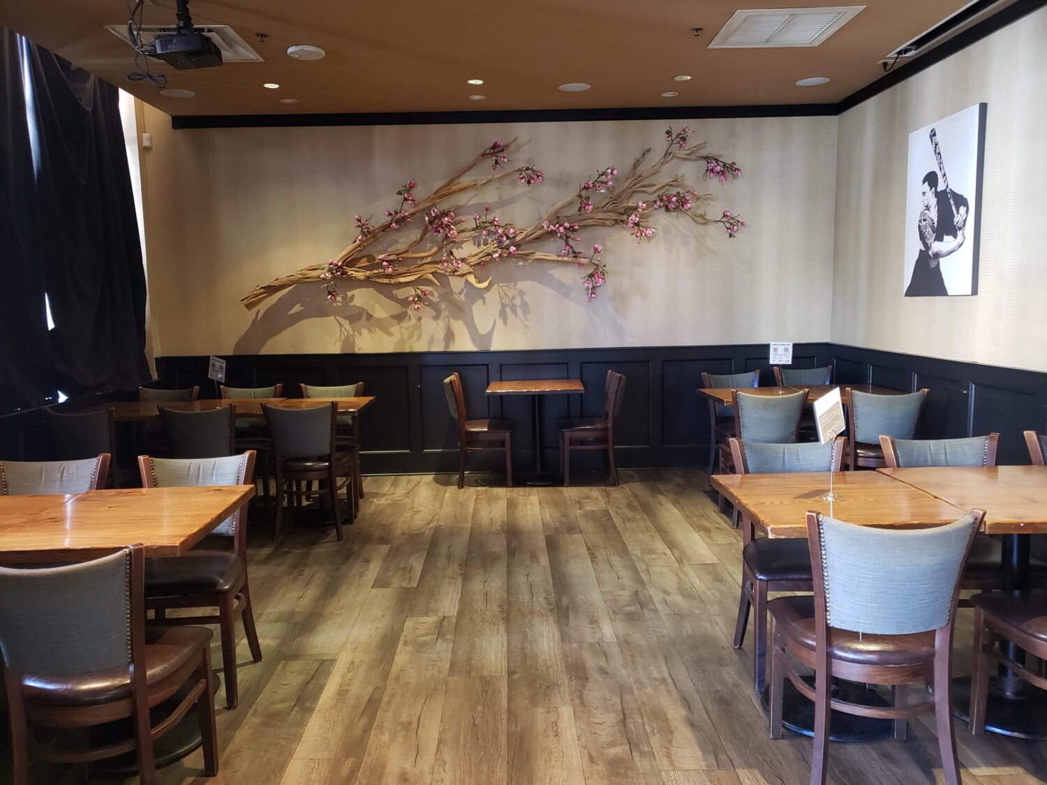 Cherry blossom art creates a serene backdrop for wooden tables awaiting their next guests – minimalist Japanese aesthetics meet Southern hospitality.