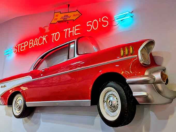 That classic car bursting through the wall captures the energy and optimism of 1950s America, frozen in cheerful perpetuity.