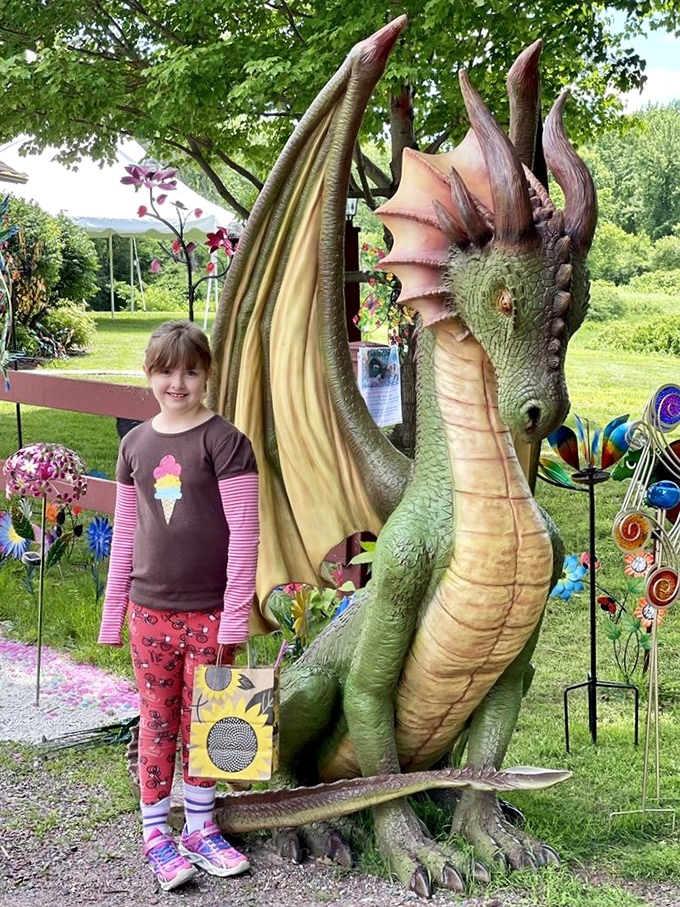 The dragon measures up! This impressive mythical creature stands tall beside a young visitor, showcasing the playful scale of The Sparkle Barn's outdoor art.