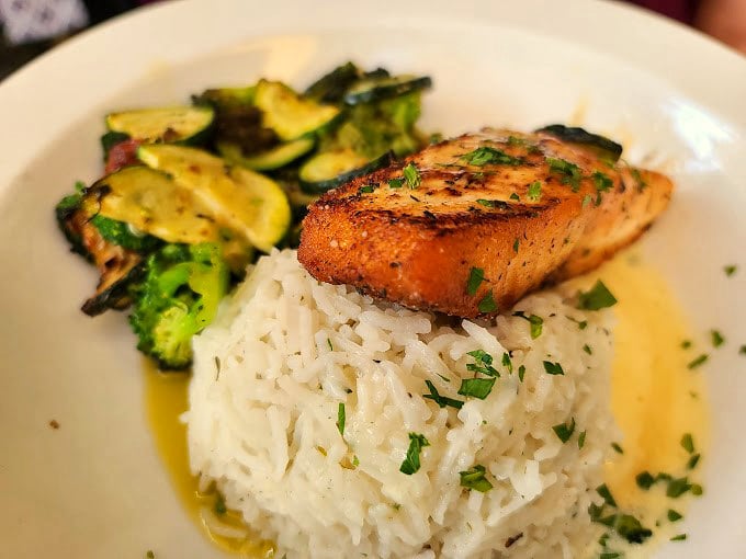 Perfectly seared fish perches atop a cloud of white rice, surrounded by vibrant vegetables in a harmony of colors and textures.