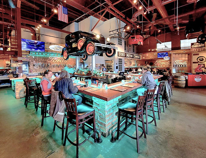 The bar area showcases an impressive craft beer selection beneath more suspended vehicles, creating a destination within the destination for beverage enthusiasts and car lovers alike.