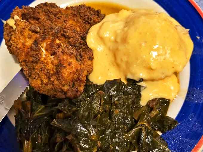 Southern comfort on a plate—crispy fried chicken alongside collards and mashed potatoes that could make a homesick Southerner weep with joy.