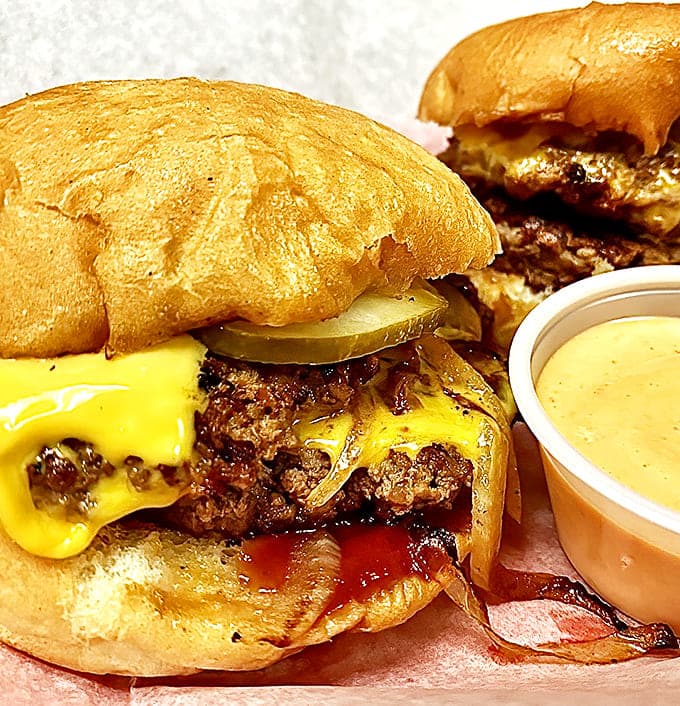 Two perfect sliders nestled side by side, their pickle sentinels and melty cheese blankets promising a flavor explosion with each bite.