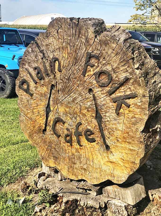 A weathered tree slice proudly displays the Plain Folk Cafe name, embodying the rustic authenticity that makes this place special.