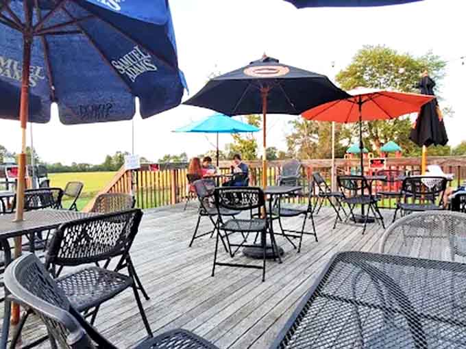 The wooden deck transforms into an oasis during warmer months, where umbrella-shaded tables offer respite and the surrounding fields provide a pastoral soundtrack.