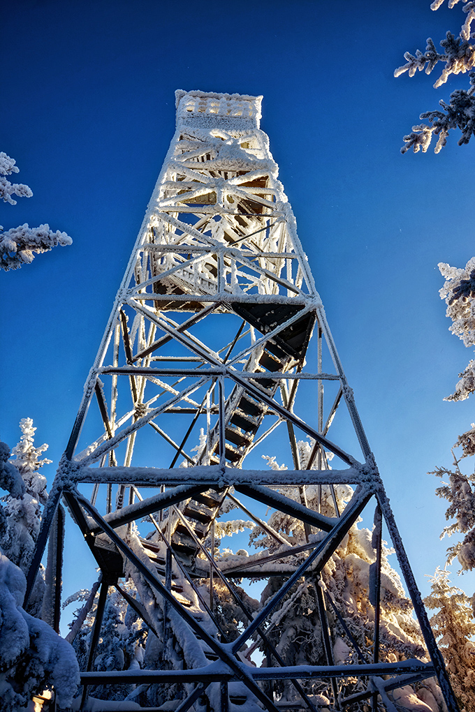 The fire tower, dressed in winter white, reaches toward an impossibly blue sky &ndash; a sentinel keeping watch over Elmore's snowy domain.