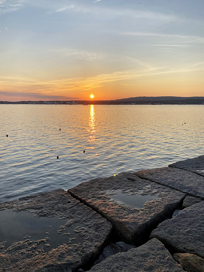 Sunset transforms Penobscot Bay into a canvas of orange and gold, with the breakwater's granite path leading the eye toward the horizon. 