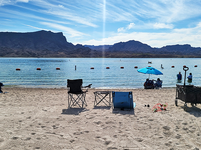 Beach chairs and coolers mark temporary territories on Cattail Cove's sandy shore, where visitors soak up Arizona sunshine with refreshing dips nearby.
