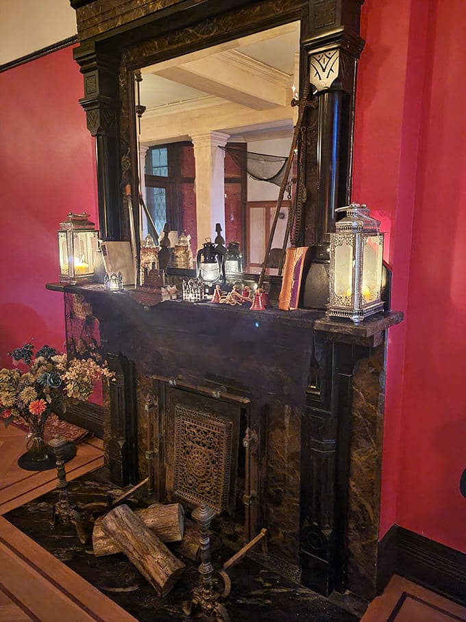 This fireplace mantel commands attention like a Victorian stage, its dark marble and ornate details framed by dramatically red walls.