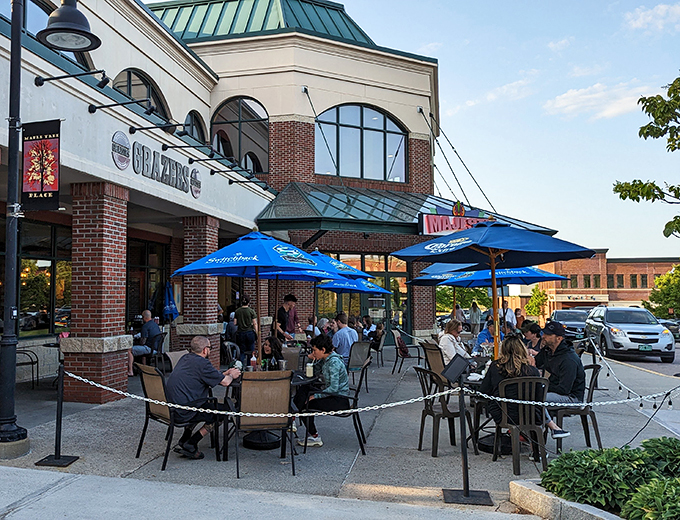 As the sun sets, the patio comes alive with diners enjoying Vermont's perfect summer evenings under blue umbrellas.