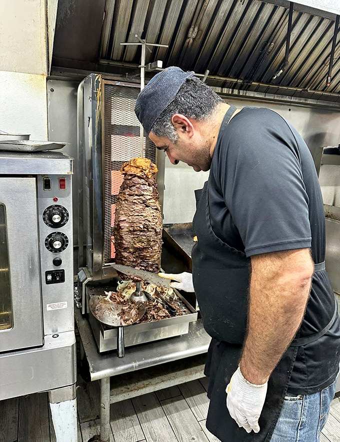 The shawarma maestro at work, carefully shaving perfectly seasoned meat from the vertical rotisserie &ndash; a culinary craftsman practicing an ancient art form.
