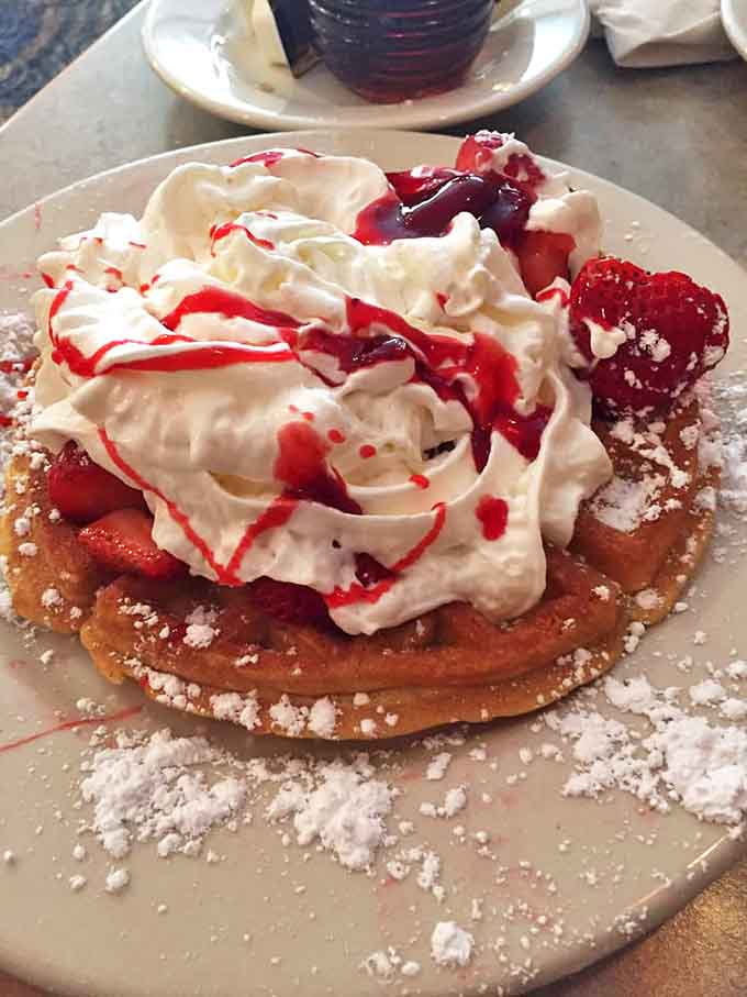 A strawberry waffle mountain topped with whipped cream and berry sauce &ndash; breakfast that doubles as a celebration on a plate.