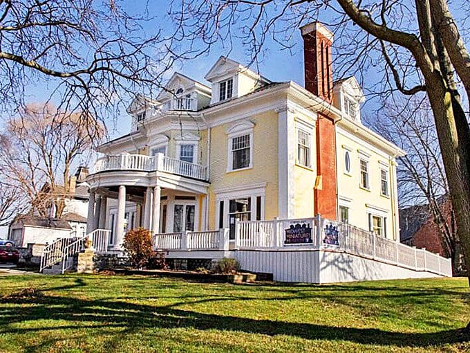 The grand yellow Victorian mansion that houses the Midwest Miniatures Museum stands elegantly against a blue sky, a perfect home for tiny treasures.