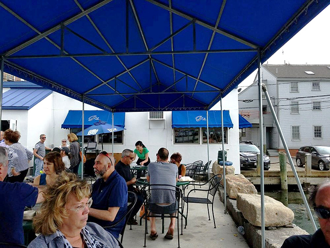 The outdoor patio, sheltered by a blue canopy, offers diners the full sensory experience of enjoying ocean-fresh seafood within earshot of lapping harbor waters.