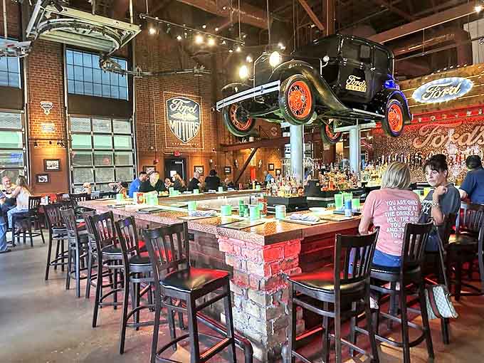 The bar area serves as command central, with a vintage Ford suspended overhead like a mechanical guardian angel watching over thirsty patrons.