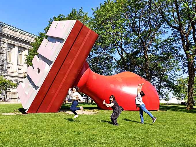 Playful visitors demonstrate the universal urge to interact with public art, pretending to push against the massive tilted sculpture.
