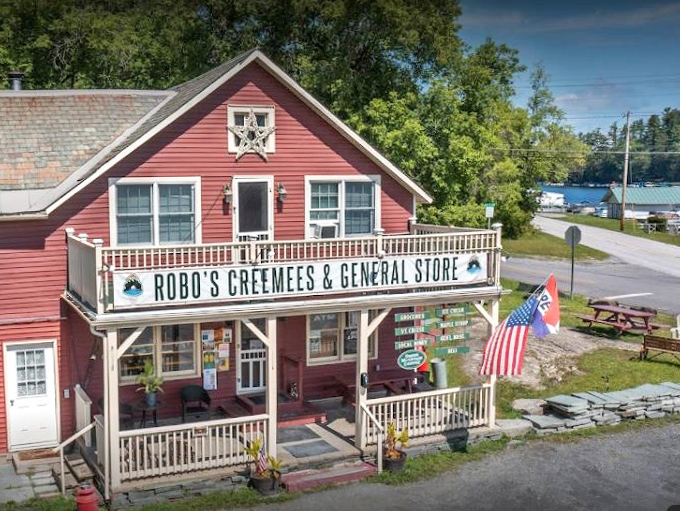 Summer sunshine bathes the general store in golden light, American flag waving gently as customers come and go through the welcoming doors.