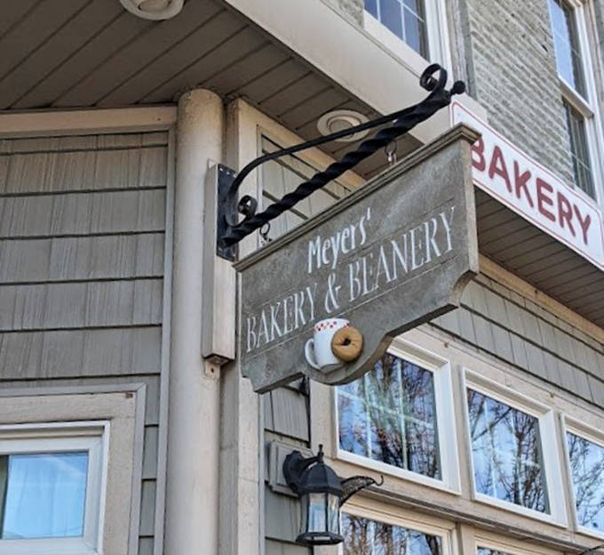 The vintage sign swinging gently outside promises simple pleasures within – a coffee cup and donut icon that speaks volumes about priorities.