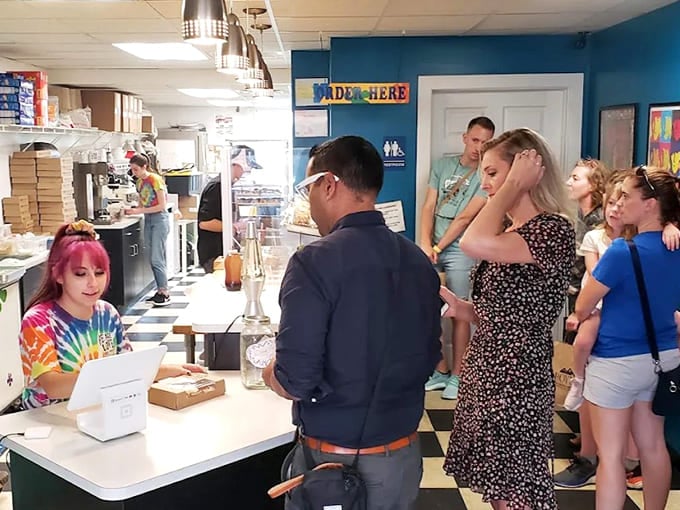 The bustling counter scene shows happy customers making tough decisions while tie-dye-clad staff prepare fresh batches of mini delights.