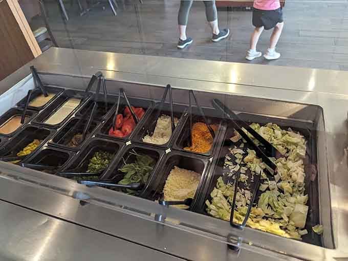 The salad bar stands ready with fresh toppings, offering lighter options for those who want vegetables before diving into pizza.