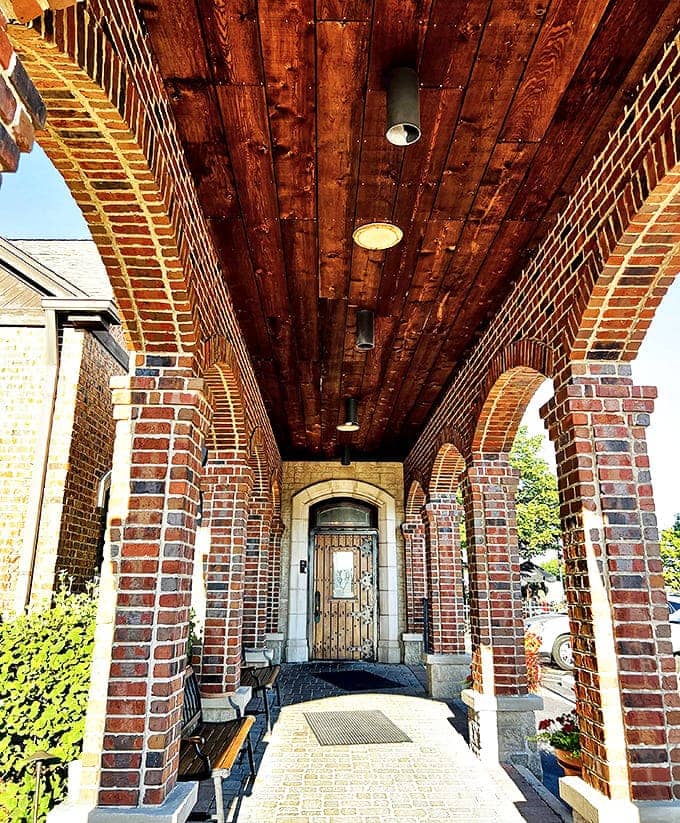 The arched brick entryway feels like a portal to another time, with wooden ceiling beams completing the old-world charm.