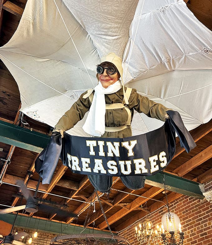 The store's whimsical mascot takes flight overhead, complete with goggles and adventure gear. This parachuting figure watches over "Tiny Treasures" with eternal optimism.