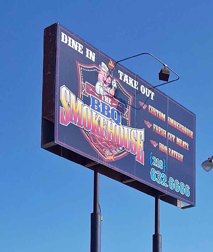 The roadside sign with its cheerful cartoon pig promises custom smokehouse, fresh cut meats, and a BBQ eatery that delivers on every word.