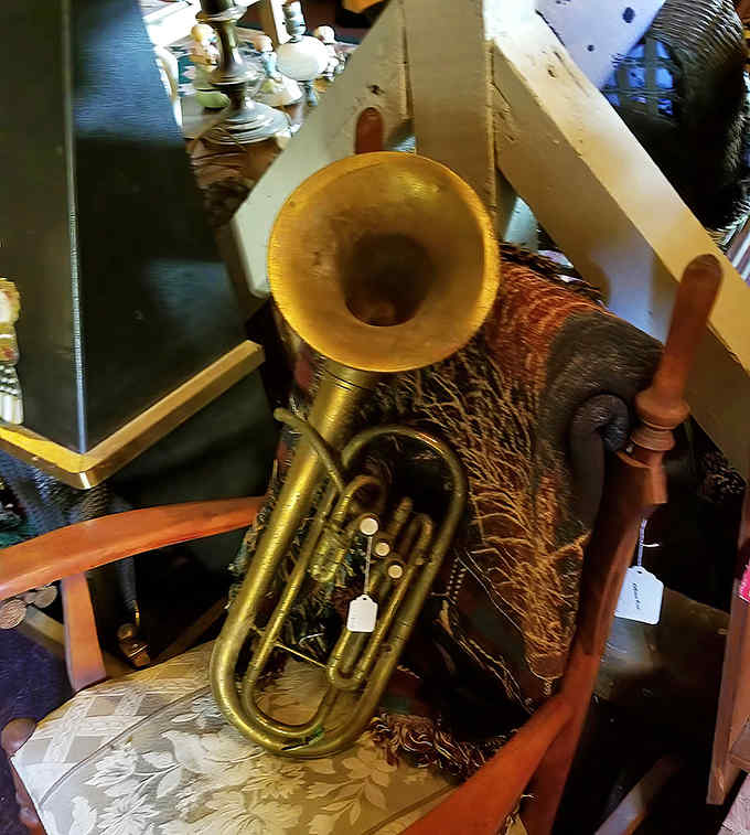 A brass baritone horn rests against vintage furniture &ndash; silent now, but imagine the music it once played at parades and community celebrations.