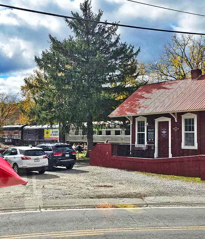 The Peninsula depot's parking area fills with cars as visitors arrive, the vintage train cars visible beyond&mdash;promising an escape from ordinary travel.