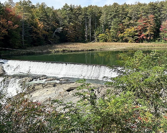 A calm river spills gently over Dewey’s Mills Dam, surrounded by colorful autumn trees that make Quechee Gorge feel peaceful and inviting.