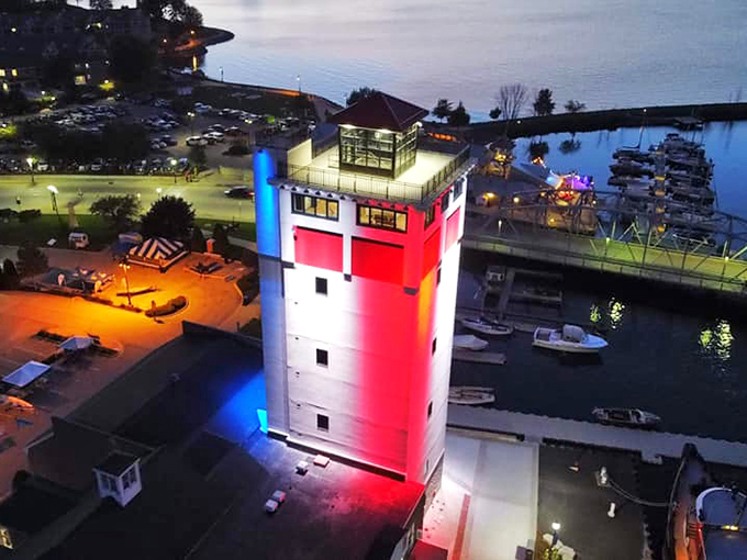 The illuminated lighthouse tower stands as a colorful beacon in the night, guiding ships and Instagram enthusiasts with equal reliability.