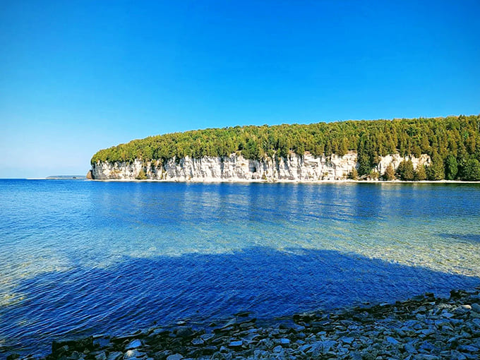 Dramatic limestone cliffs meet azure waters, showcasing the natural beauty that surrounds this remarkable ghost town frozen in time.