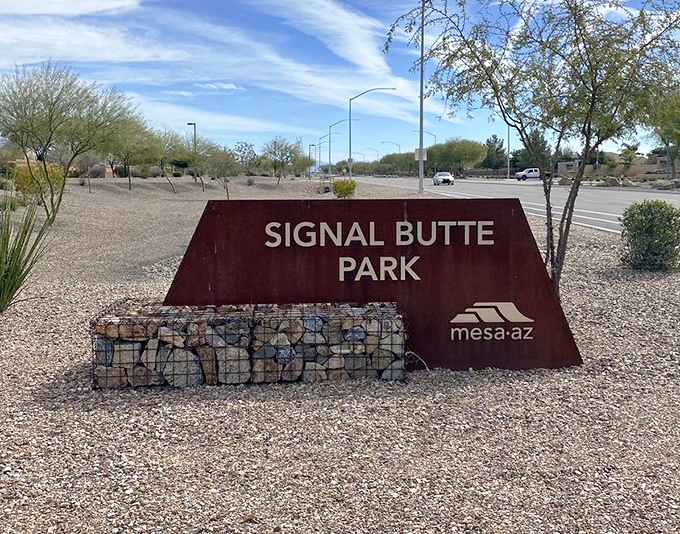 The park's entrance sign anchors visitors in place while the desert landscape stretches toward mountain views &ndash; Mesa's geometric playground awaits.