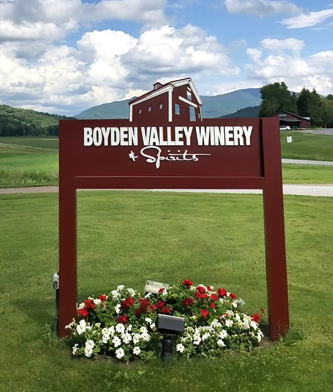 The winery's sign, surrounded by vibrant flowers, welcomes visitors to this Cambridge treasure against the breathtaking backdrop of Vermont's rolling hills.