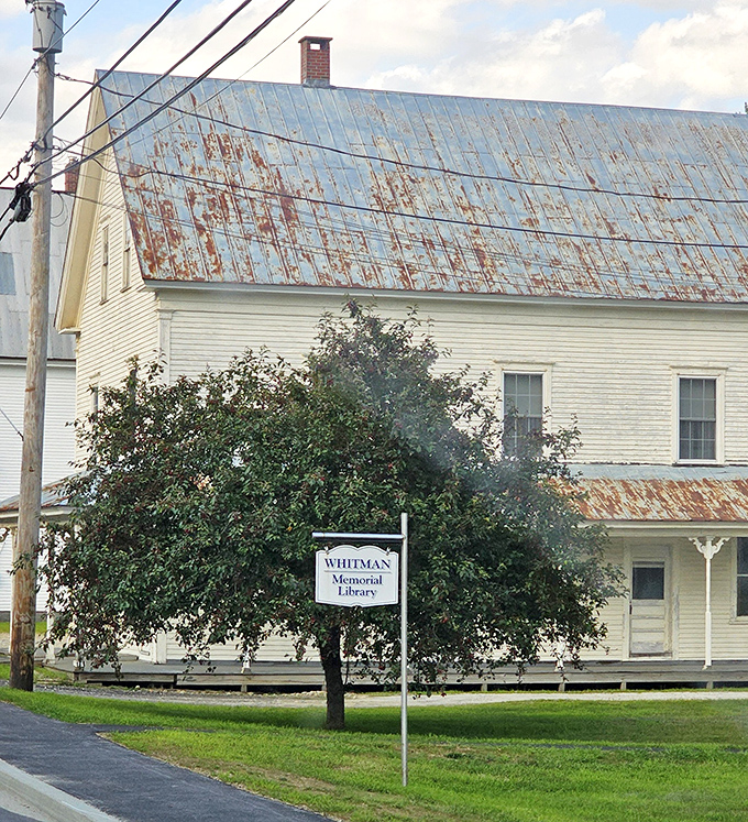 The Whitman Memorial Library stands nearby, its classic New England architecture and weathered metal roof complementing the area's historical charm.