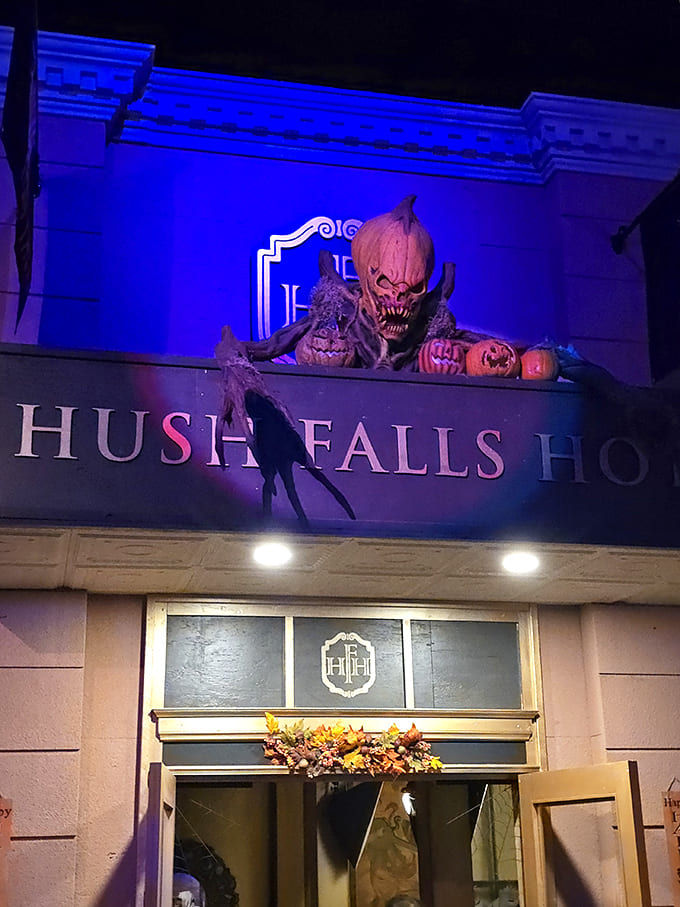 A pumpkin-headed creature looms menacingly above the Hush Falls Hotel entrance, its glowing eyes following visitors as they approach the point of no return.