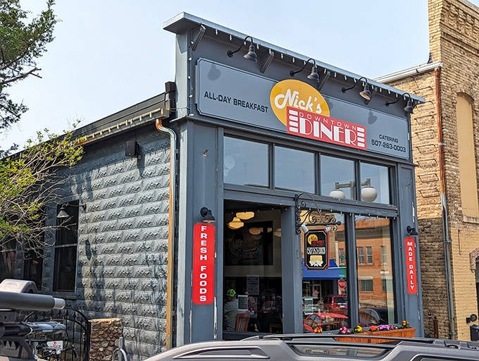 Nick's Downtown Diner's charming blue-gray exterior beckons hungry travelers with its unpretentious promise of "ALL DAY BREAKFAST" &ndash; comfort food heaven awaits inside.