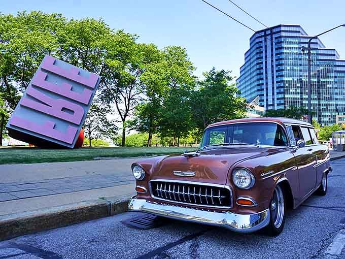 A classic vintage Chevy poses beside Cleveland's mammoth Free Stamp, two American icons sharing a moment across generations.